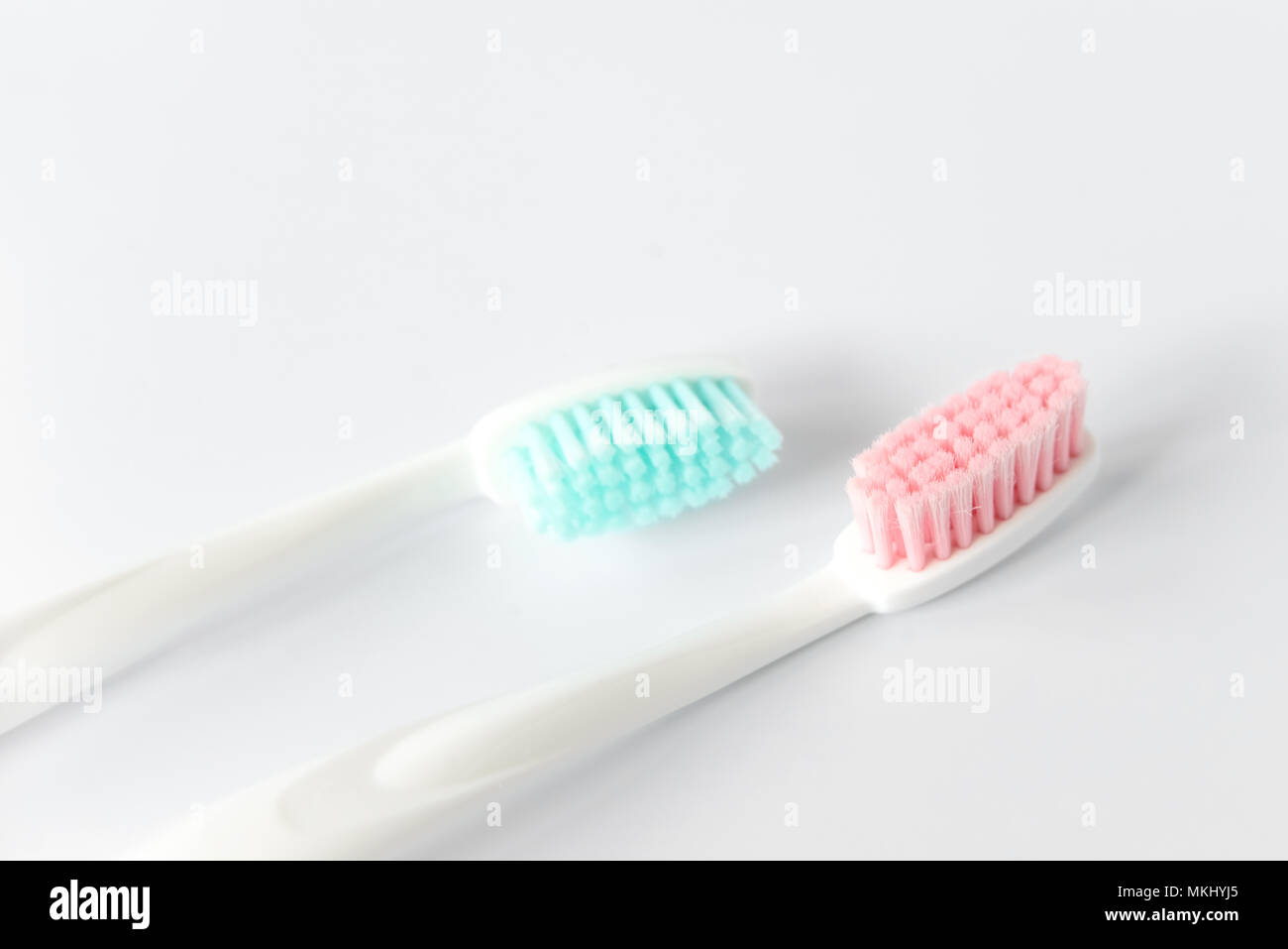 Close up of two plastic white toothbrushes with pink and blue bristle ...