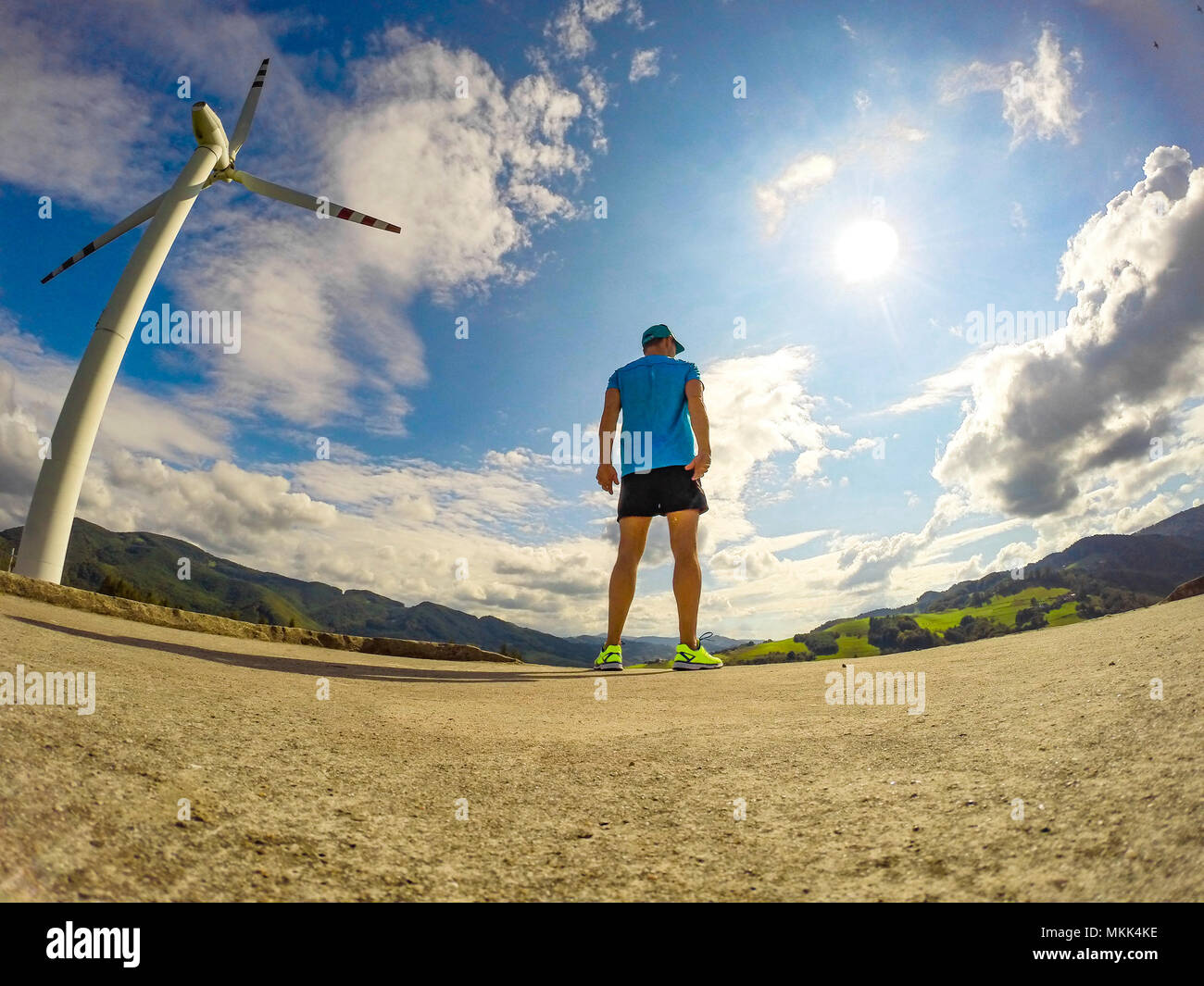 Male athlete runner standing at wind turbine and blue sky background ...
