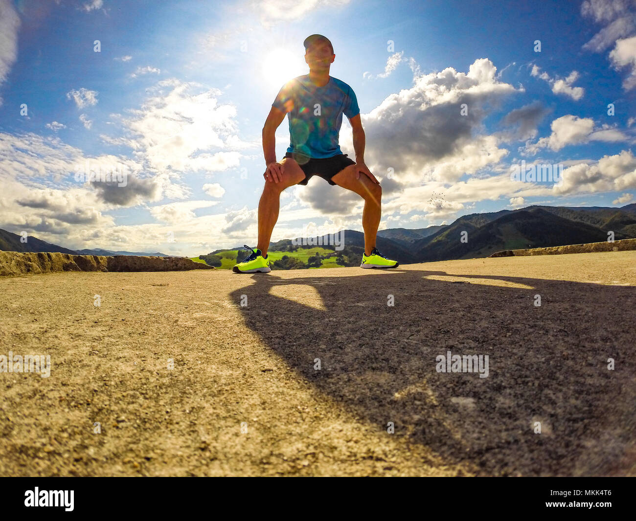 Male athlete runner stretching outdoors at sun and blue sky background ...