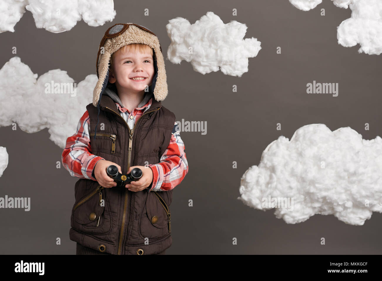 boy dressed as an airplane pilot stands between the clouds and looks ...