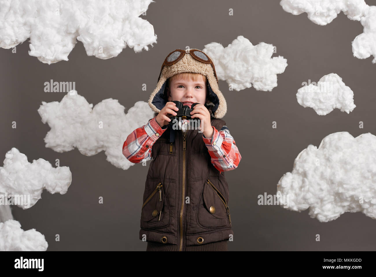 boy dressed as an airplane pilot stands between the clouds and looks ...