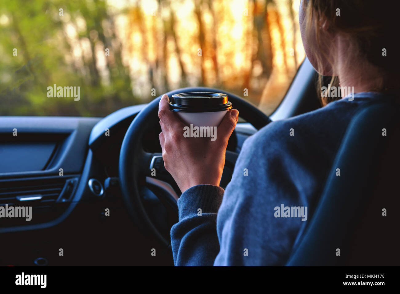 A young woman drinks coffee while driving a car while traveling. The ...
