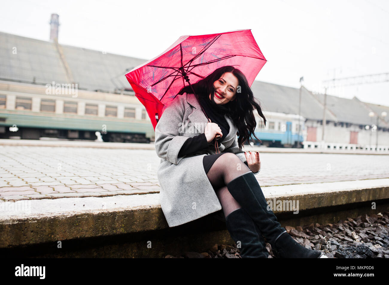 Brunette girl in gray coat with red umbrella in railway station Stock ...