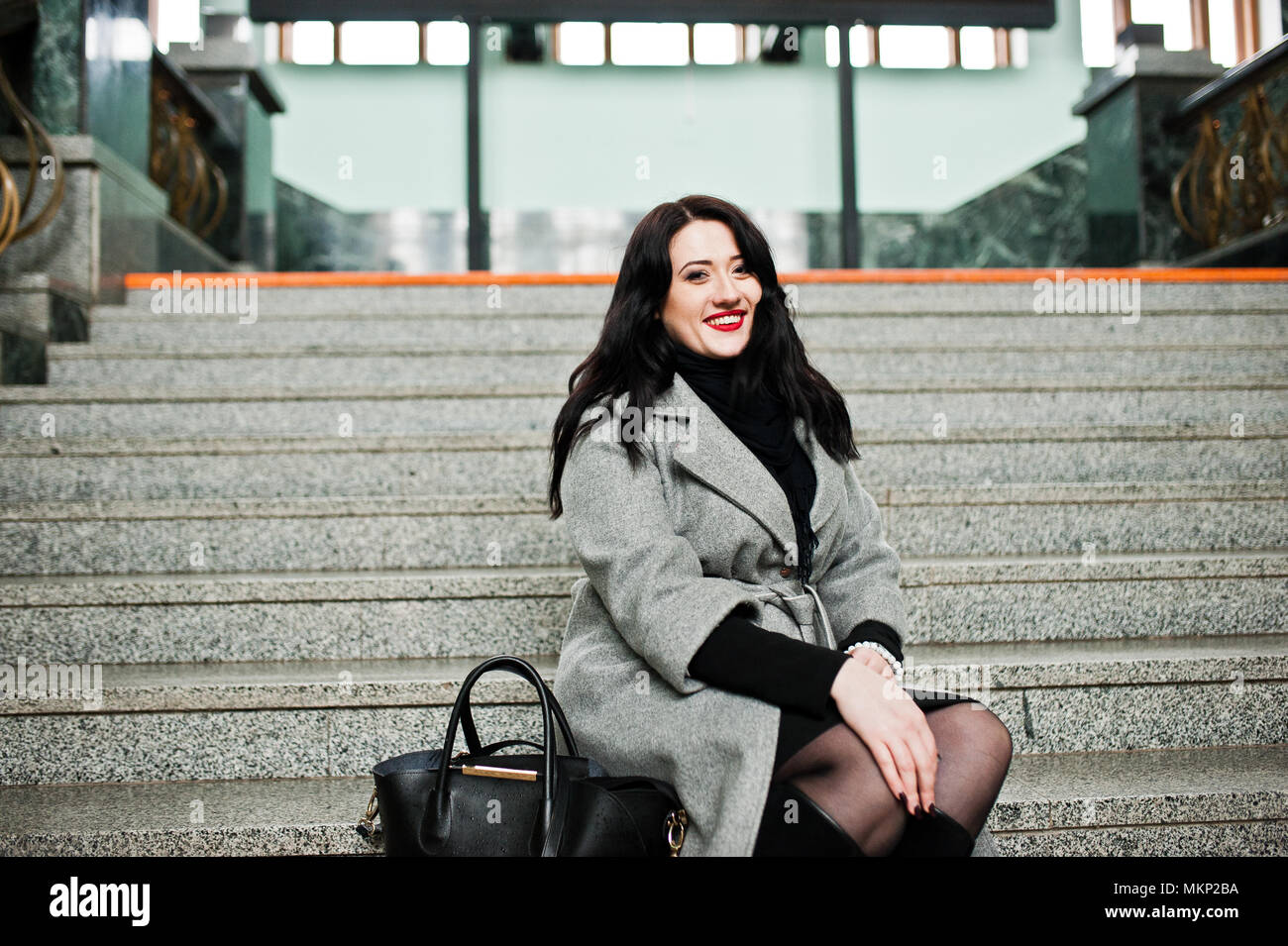 Brunette girl in gray coat posed in stairs of railway station indoor ...
