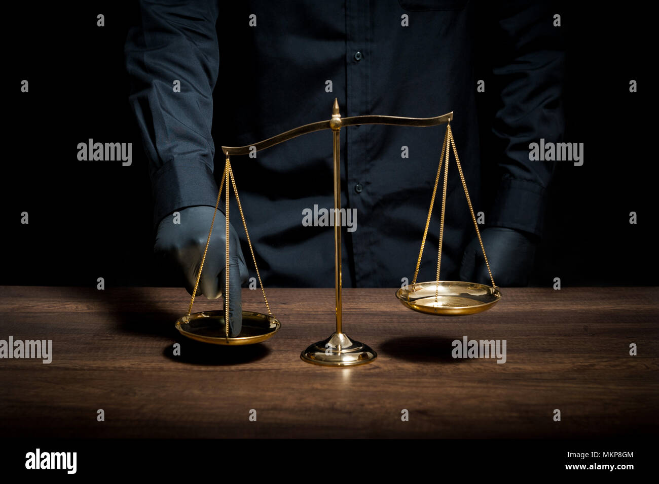 Man in black shirt with black glove pushing on scale of justice in dark ...