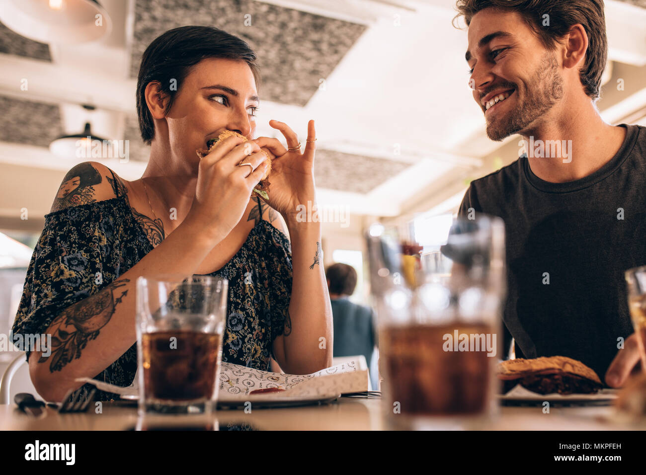Woman hanging out with her boyfriend and eating burger. Couple sitting ...