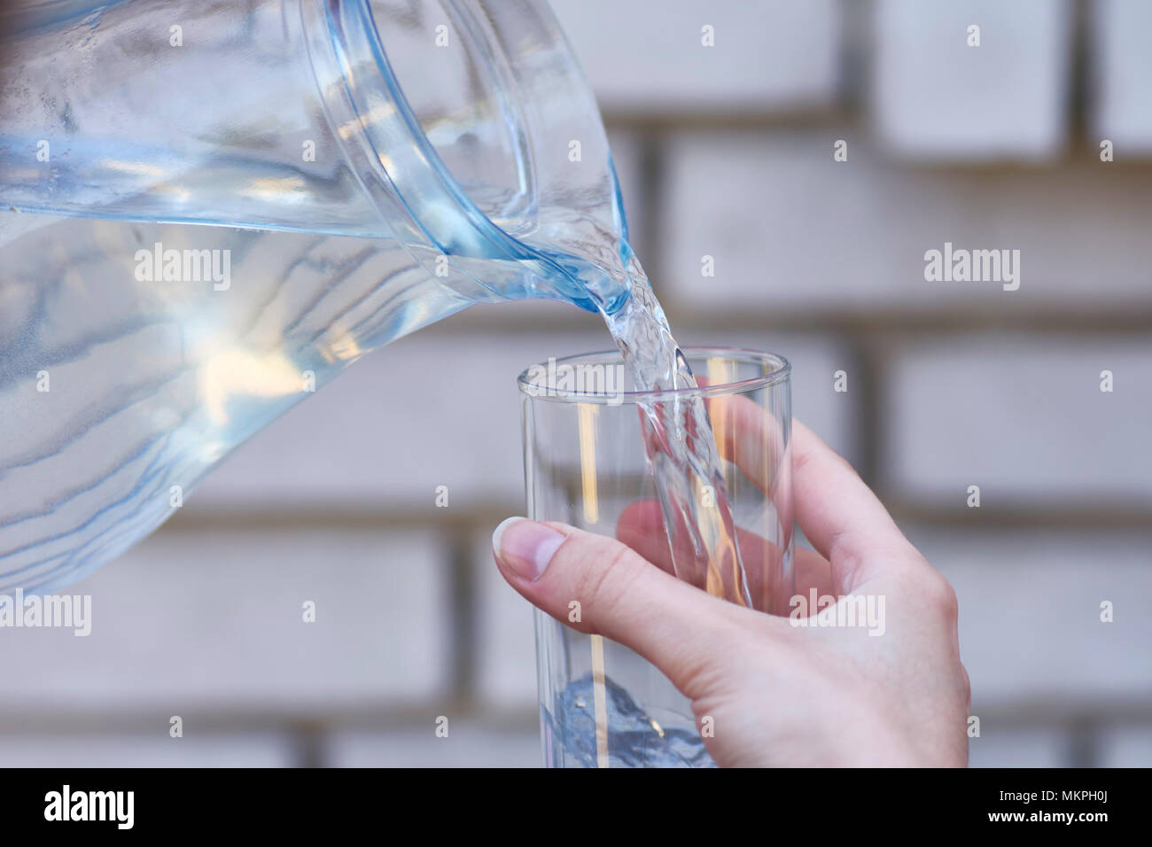 Female hand holding a glass, pouring water out of a pitcher, with a ...