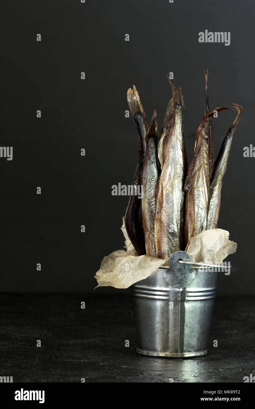 Capelin cold smoked fish in a decorative bucket on a dark background ...
