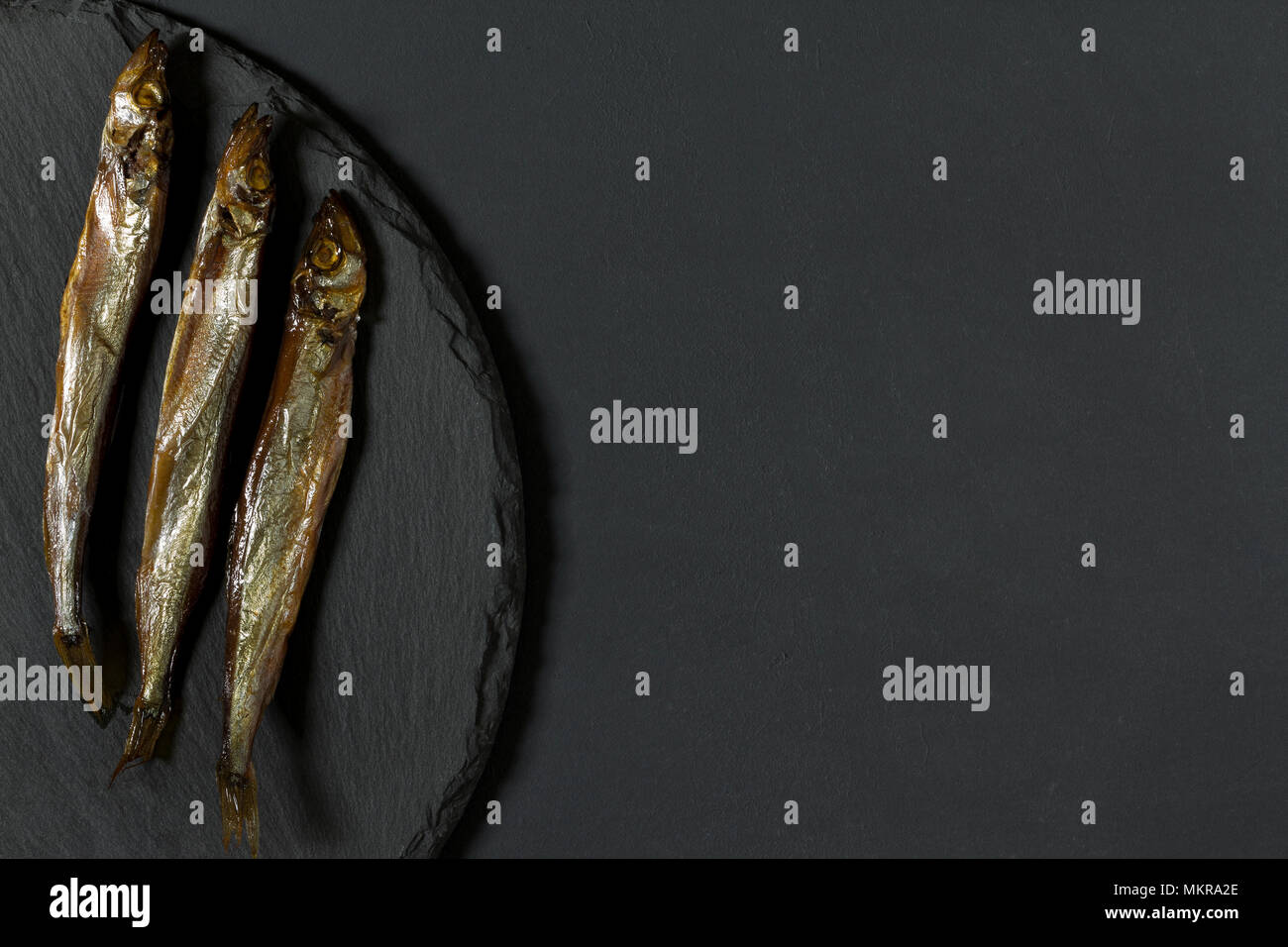 Capelin fish of cold smoked on round slate plate on black background ...