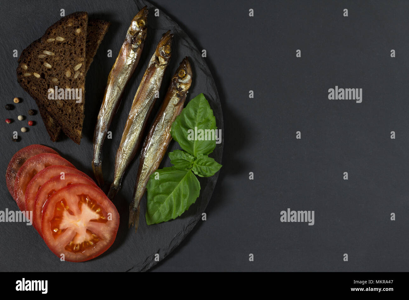 Capelin fish of cold smoked on round slate plate on black background ...