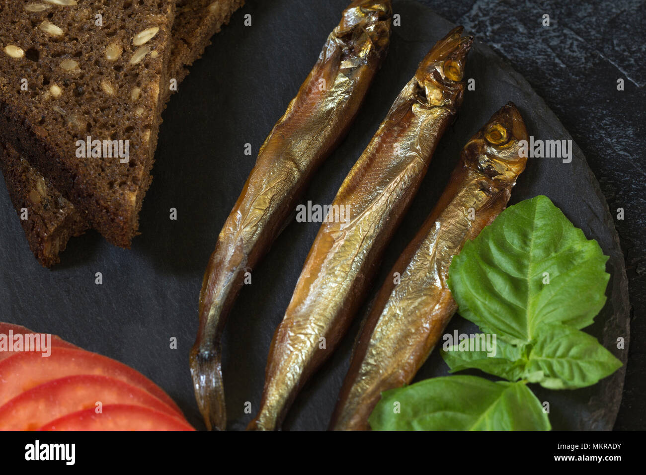 Capelin cold smoked fish on a round slate plate on a black-gray rough ...
