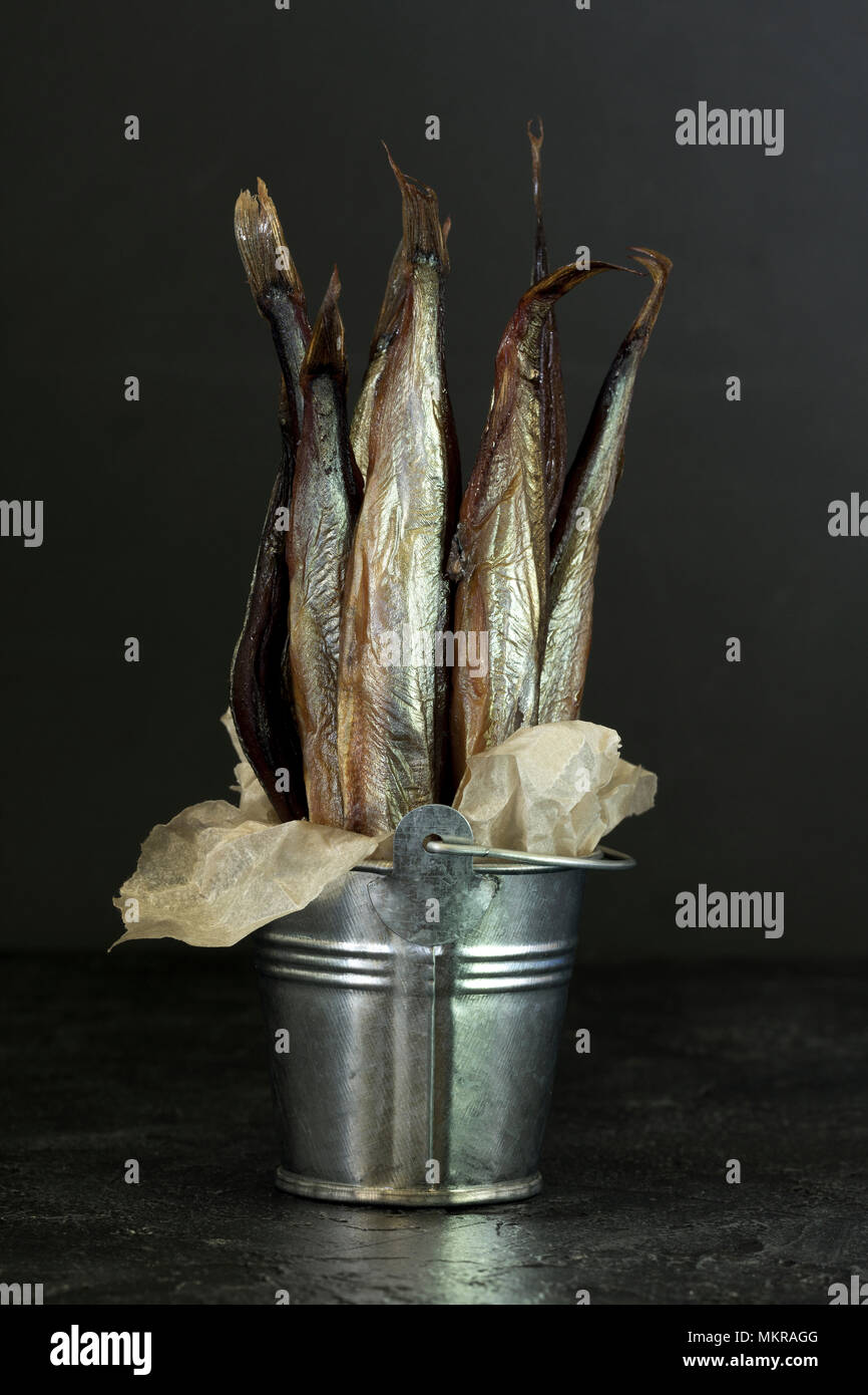 Capelin cold smoked fish in a decorative bucket on a dark background ...