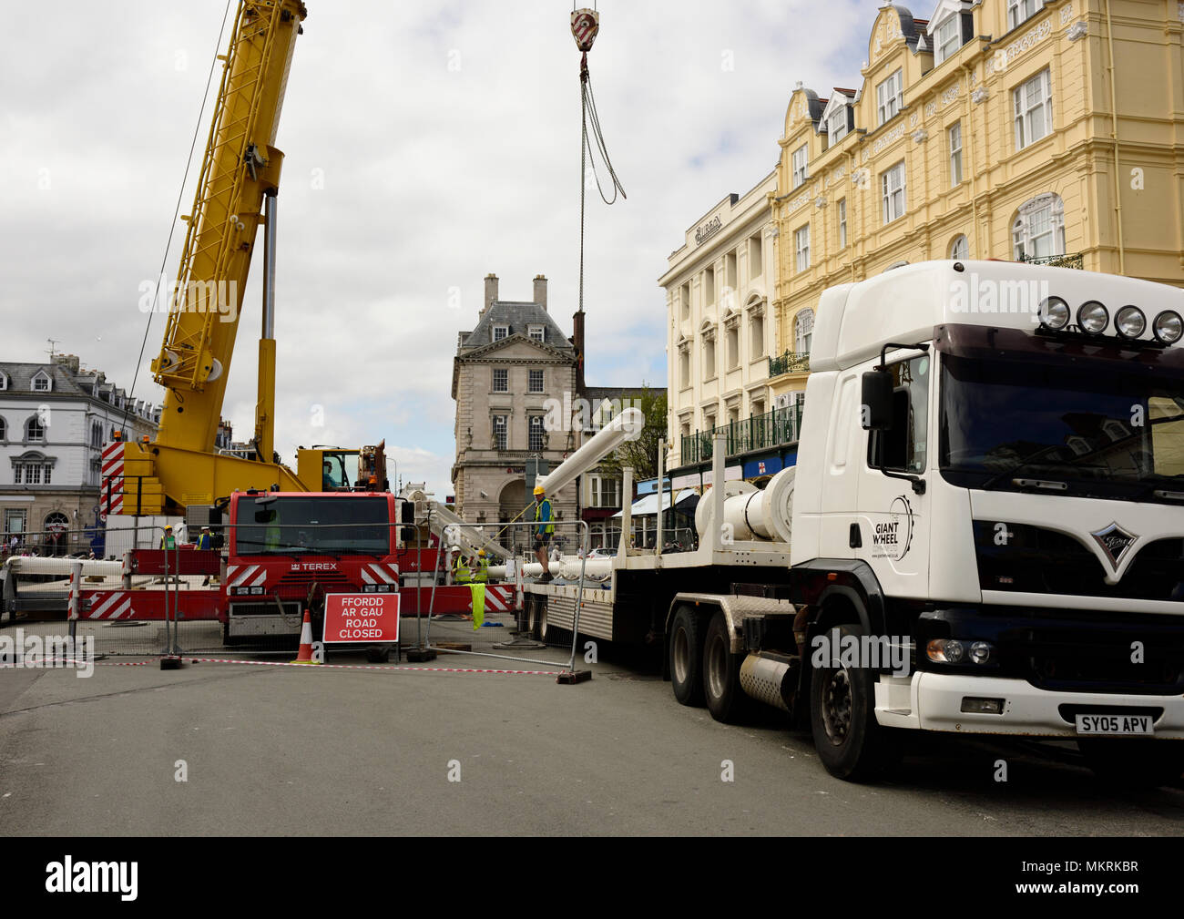 Mobile crane lifting heavy steel tube off low loader lorry behind ...