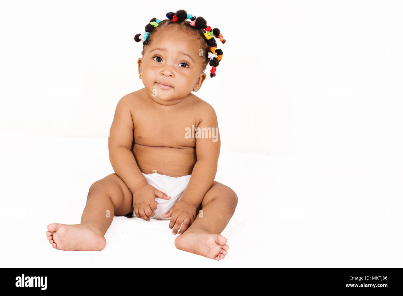 Portrait of a baby girl sitting, pulling her nappy and looking at the ...