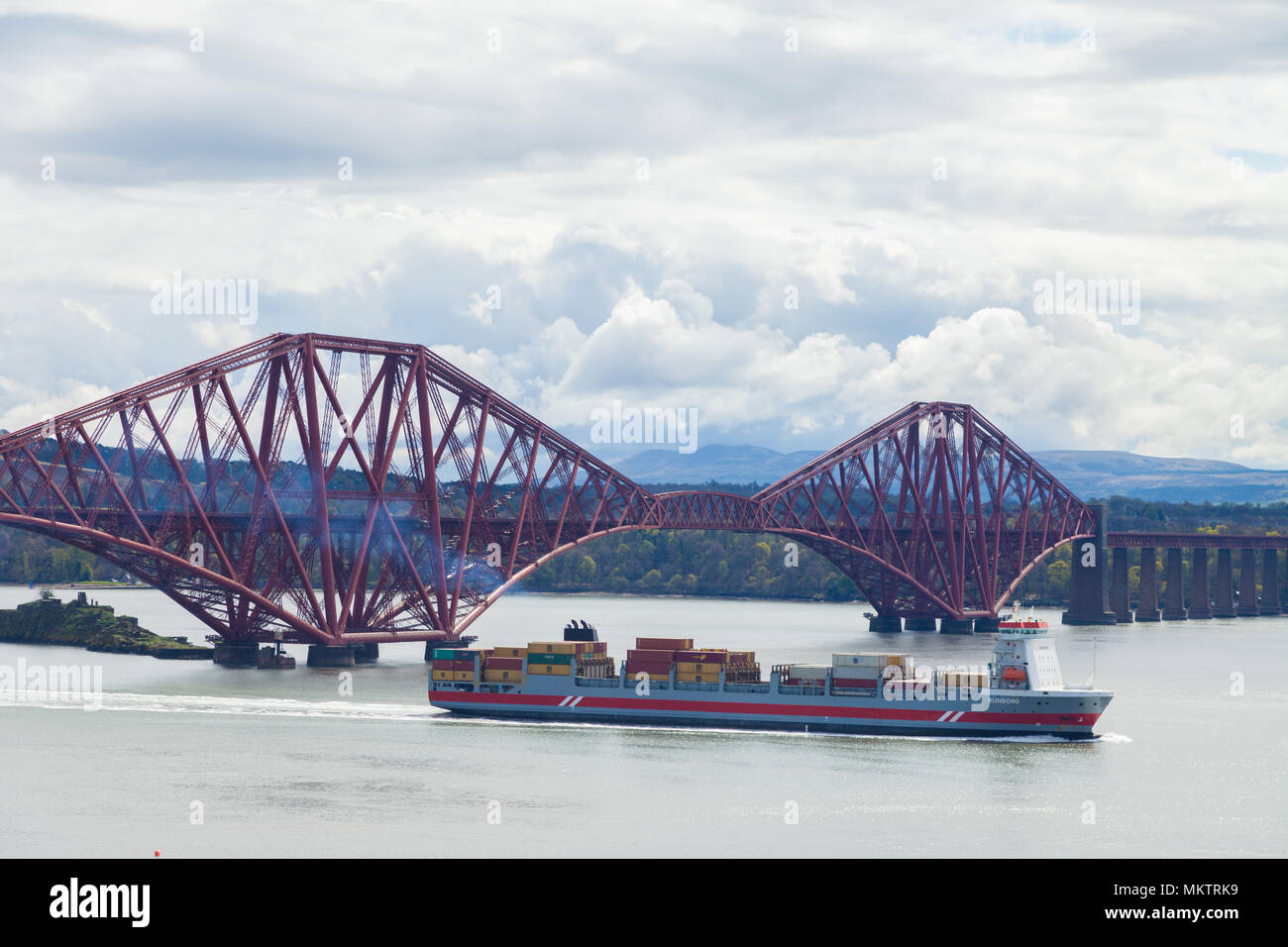 A cargo boat passing under the Forth rail Bridge near Edinburgh ...