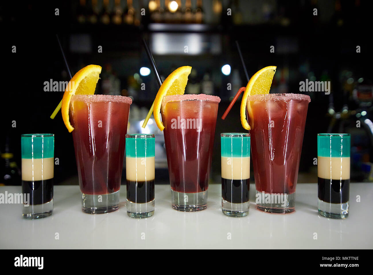 Multicolored shots and cocktails on a bar counter against a dark ...