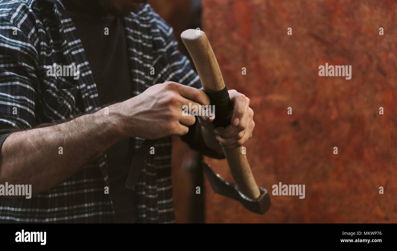 Man working in carpentry workshop. He wraps wooden handle of ax with ...