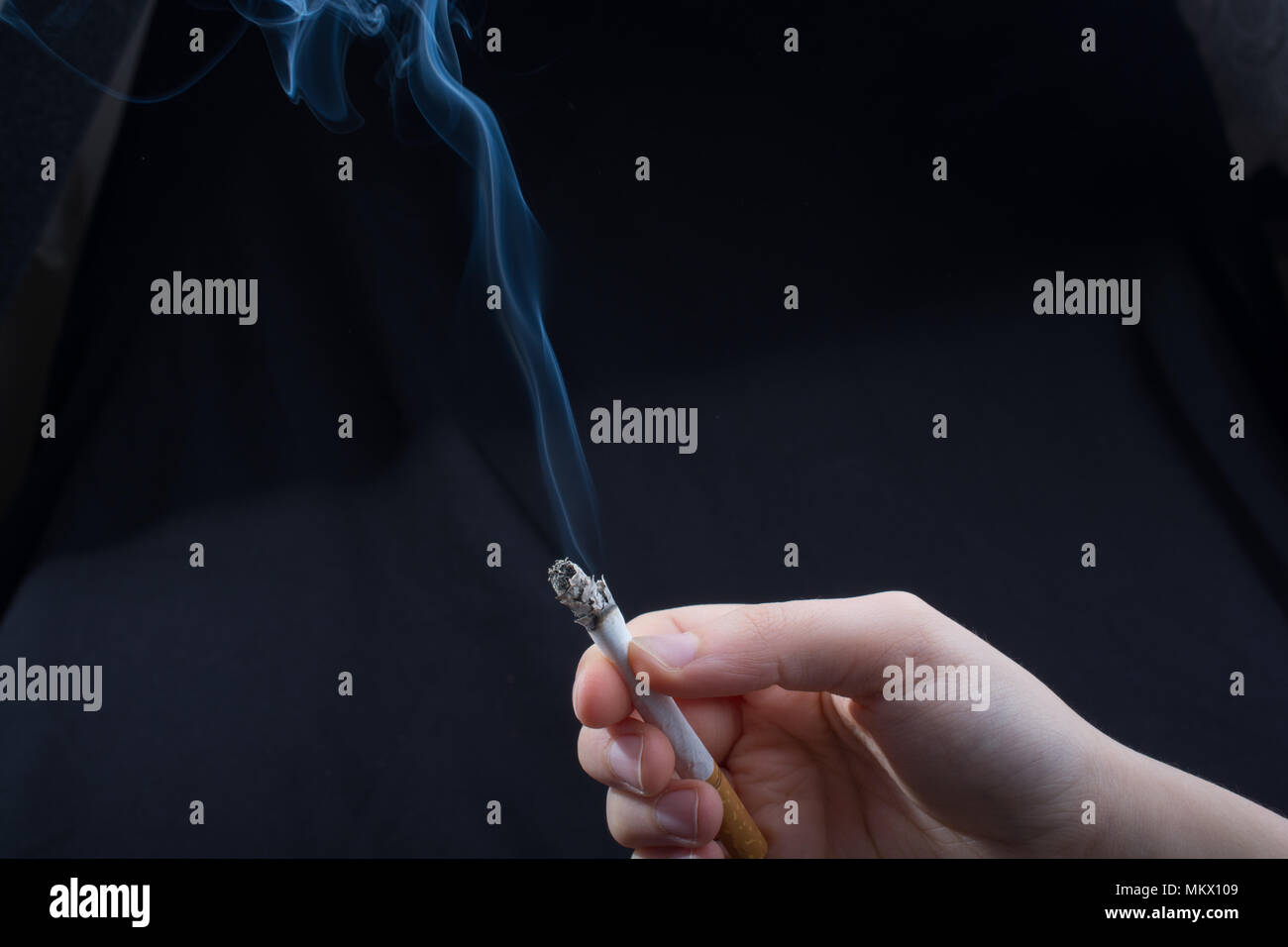 Hand is holding smoking cigarette with smoke around Stock Photo - Alamy