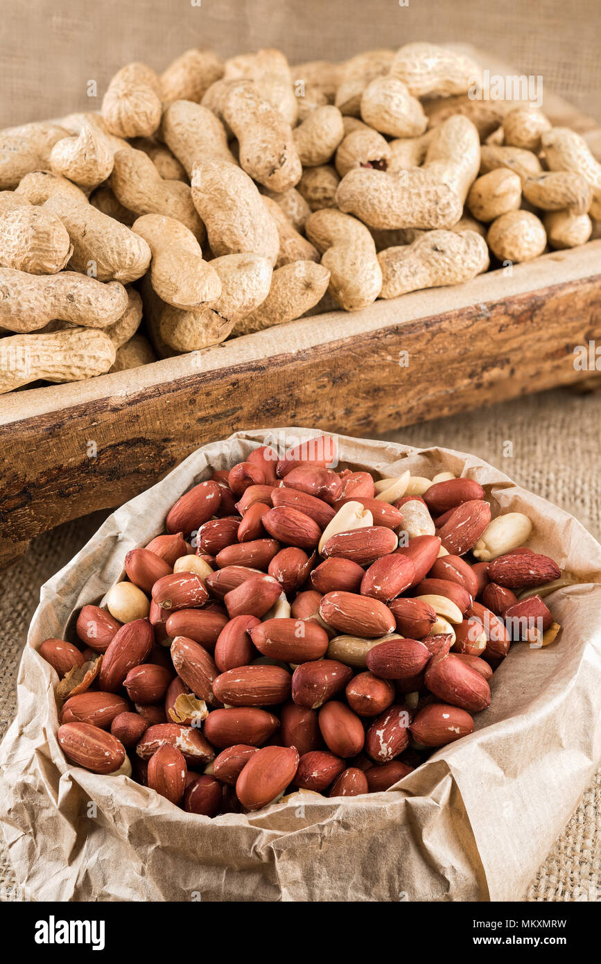 Paper bag full of peeled peanuts and peanuts in nutshell on a piece of ...
