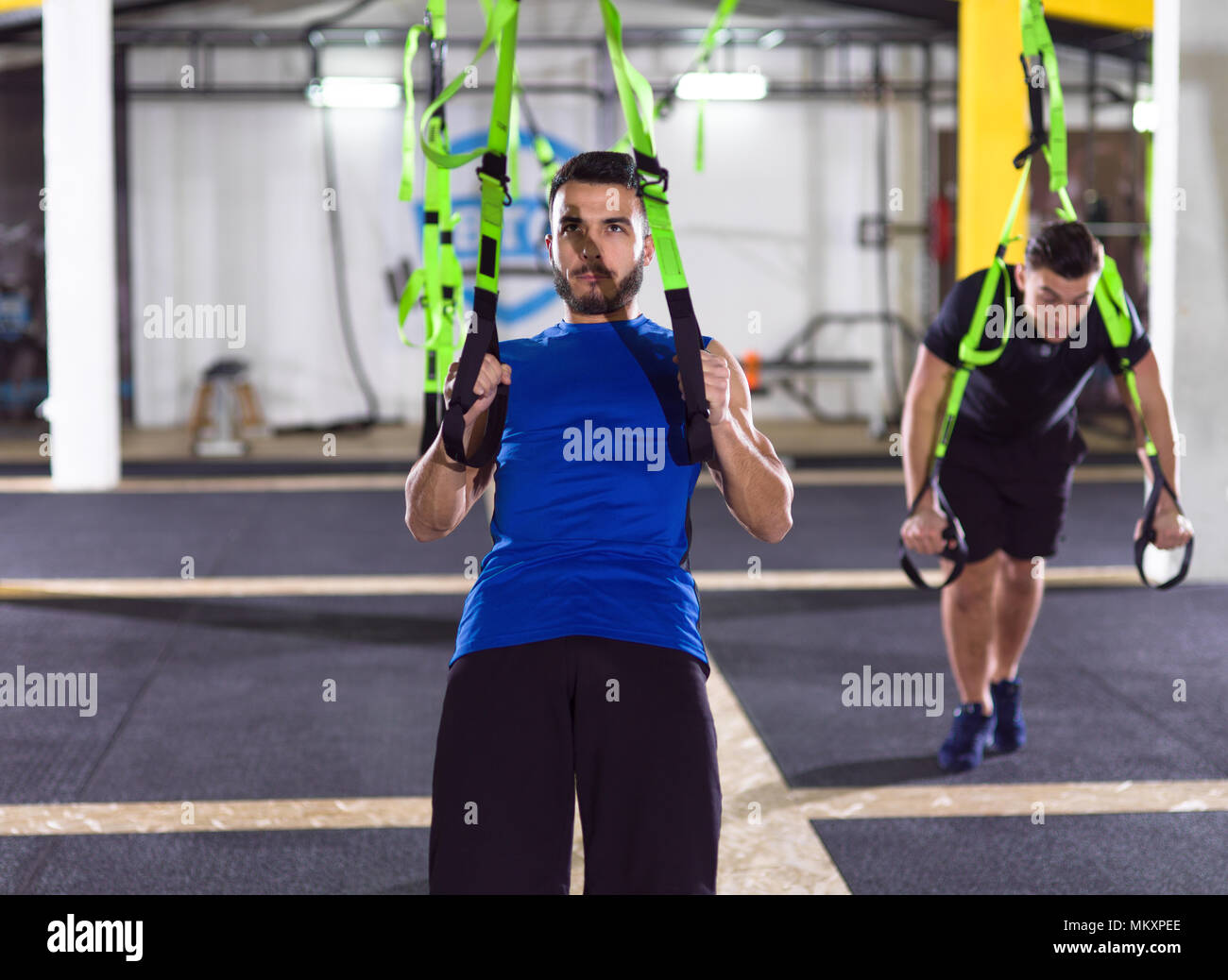 two young athlete men working out pull ups with gymnastic rings at the ...
