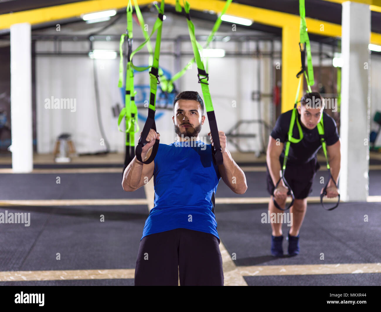 two young athlete men working out pull ups with gymnastic rings at the ...