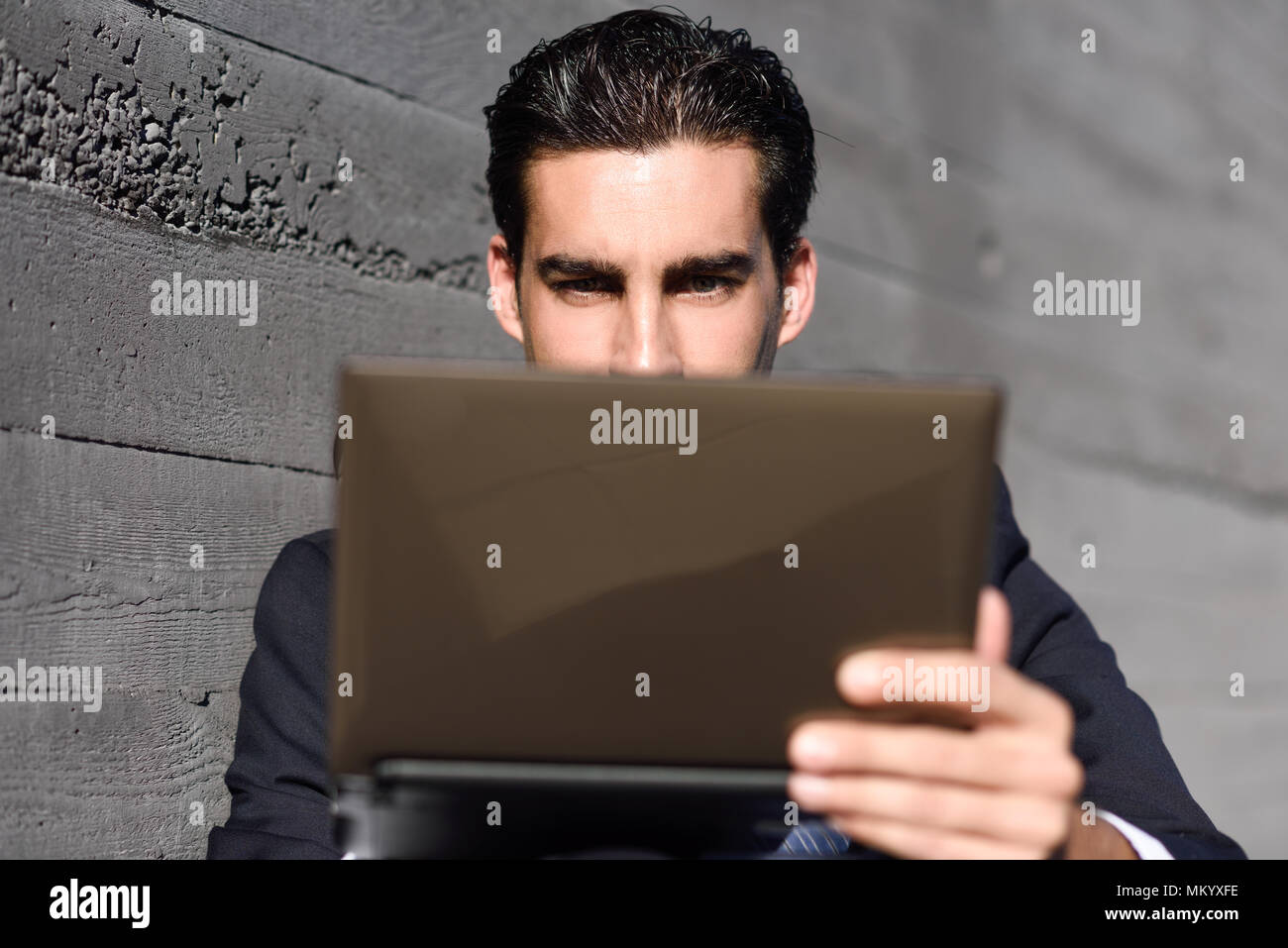 Good looking businessman using a laptop computer sitting in the street ...