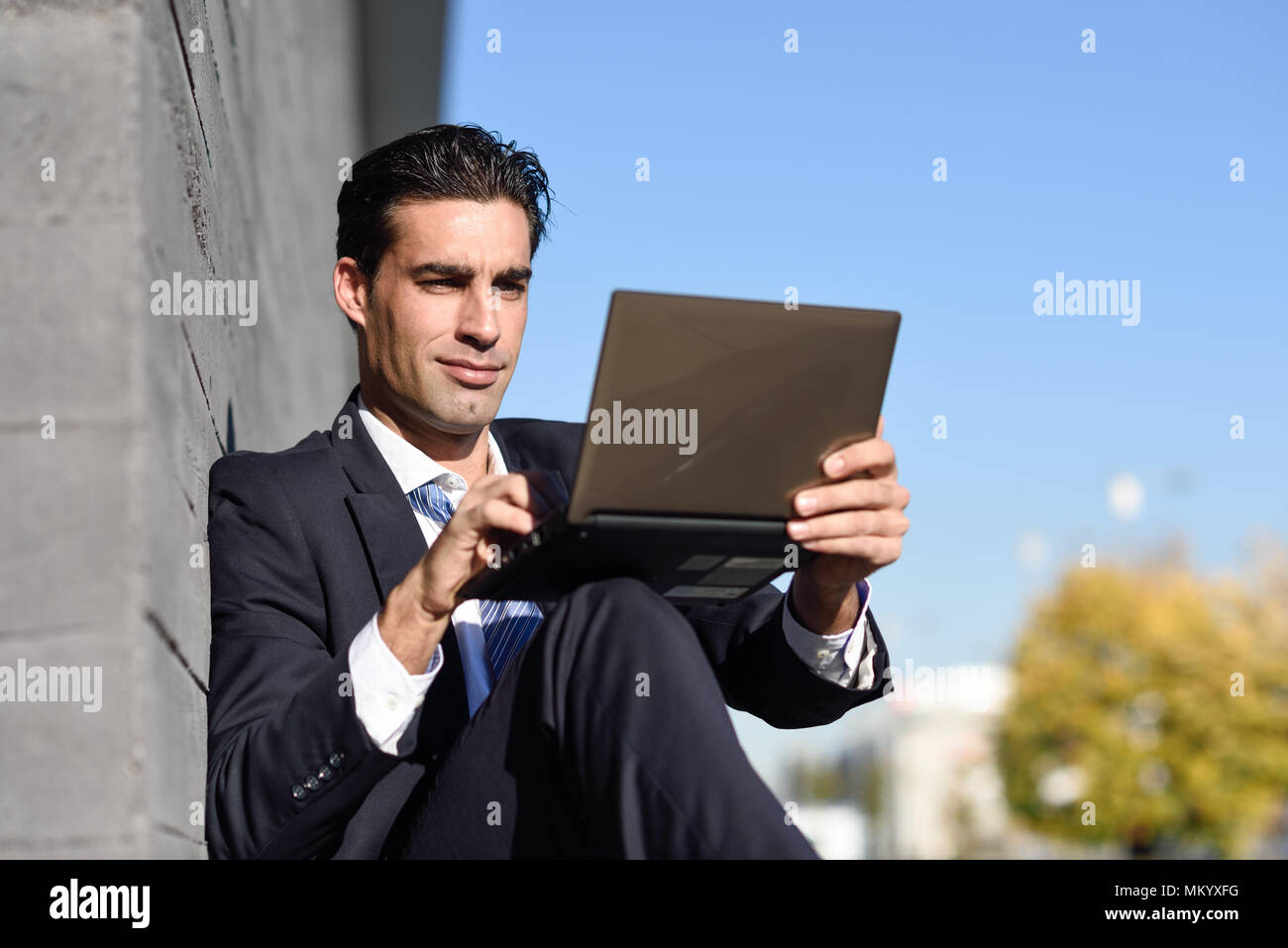 Good looking businessman using a laptop computer sitting in the street ...