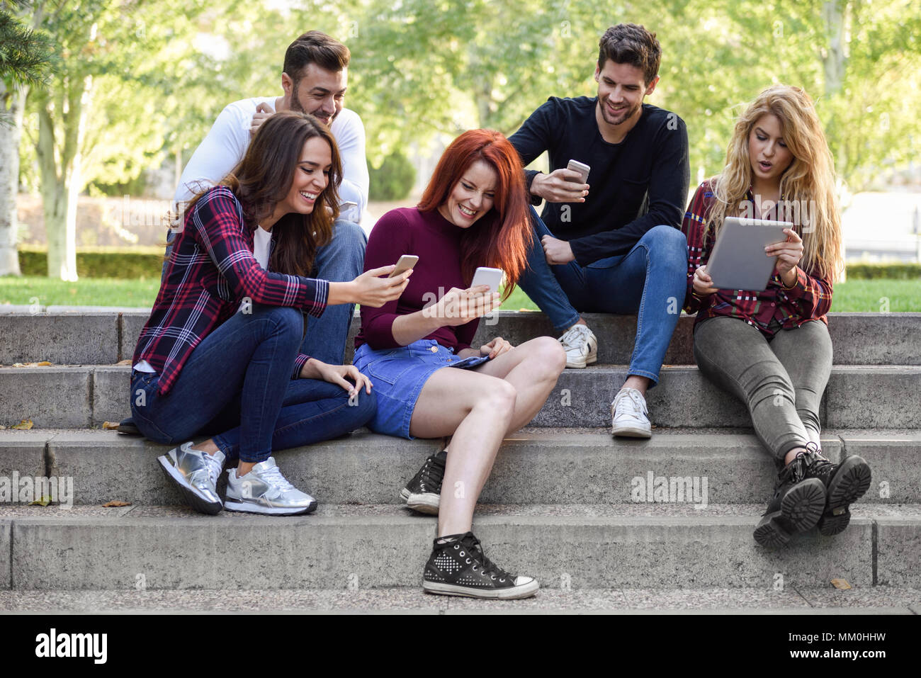 Group of young people using smartphone and tablet computers outdoors in ...