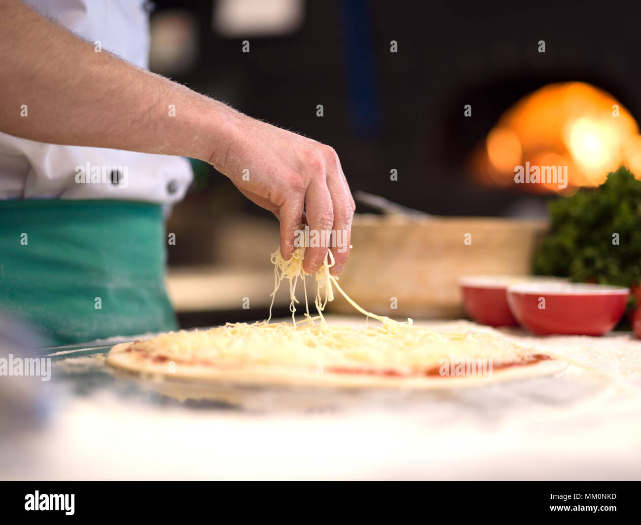 chef sprinkling cheese over fresh pizza dough on kitchen table Stock ...