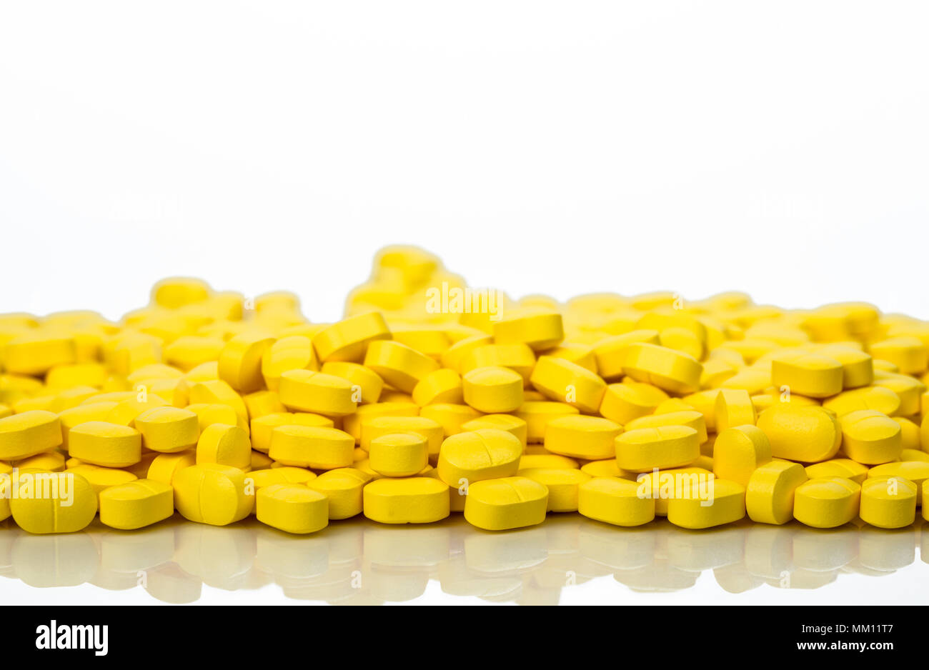Pile of yellow ovoid-rectangular shape tablet pills isolated on white ...