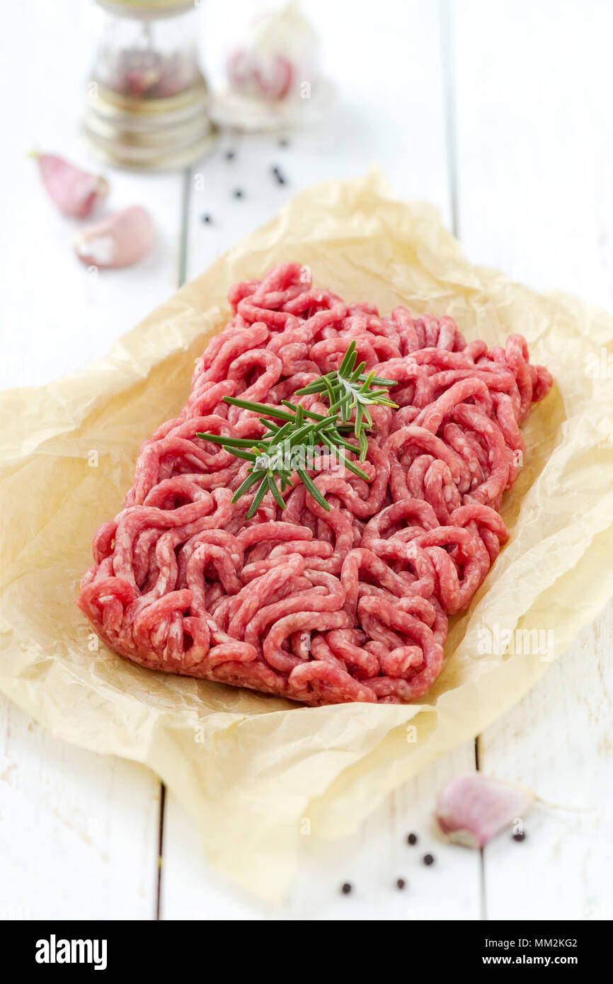 Fresh mince or ground beef meat on parchment paper with rosemary sprig ...