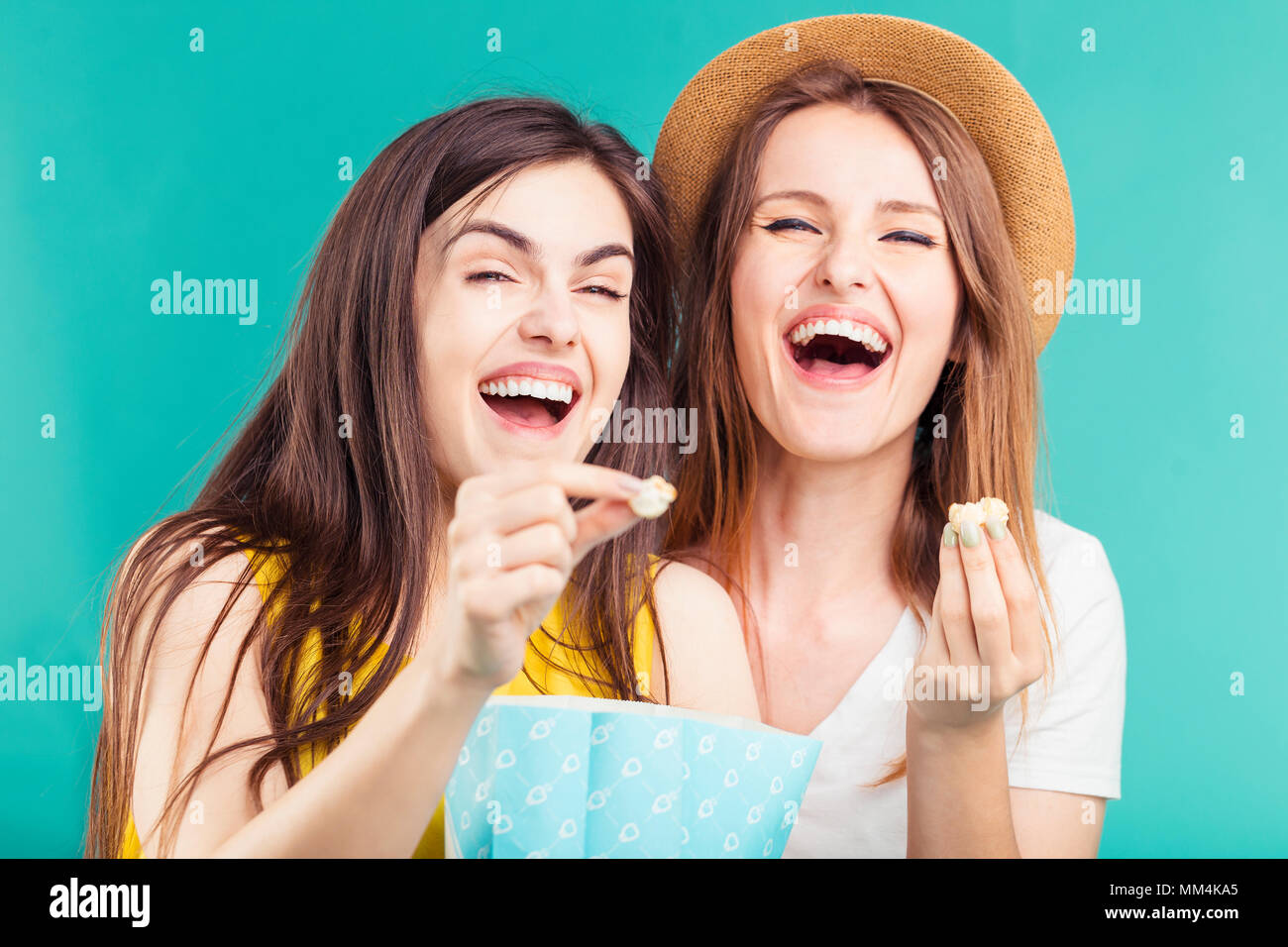Two pretty smiling girls having fun watching film with pack of popcorn ...