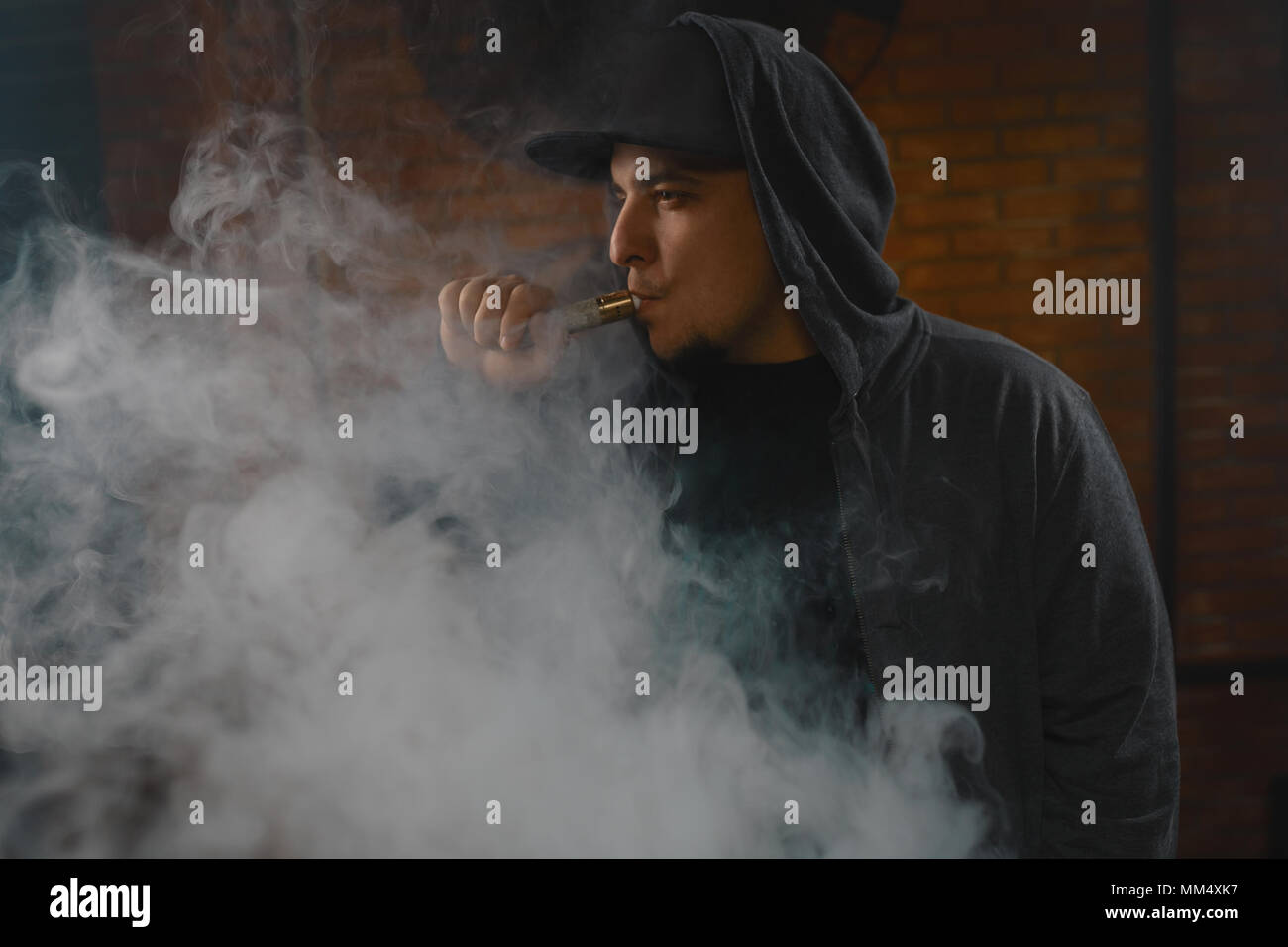 A cloud of vapor. Vaping man holding a mod. Brick background. Vape ...