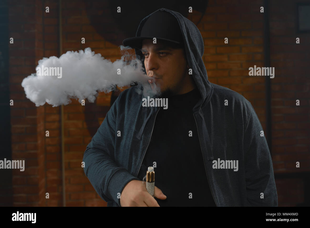 A cloud of vapor. Vaping man holding a mod. Brick background. Vape ...