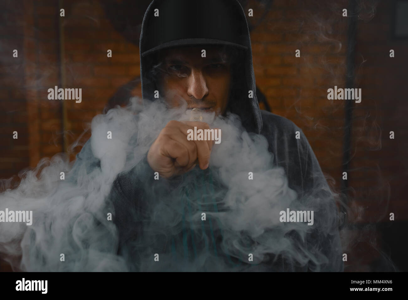 A cloud of vapor. Vaping man holding a mod. Brick background. Vape ...