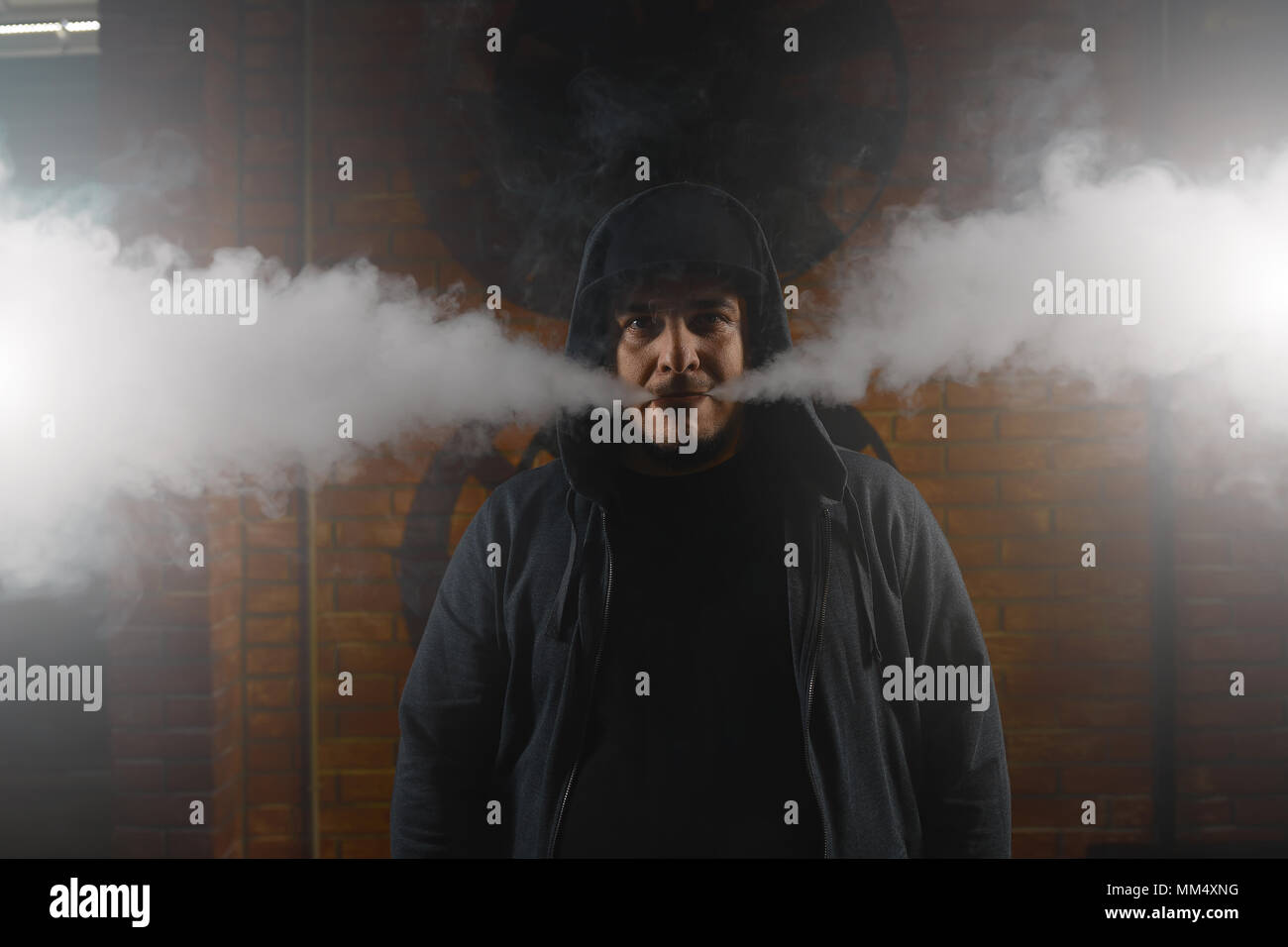A cloud of vapor. Vaping man holding a mod. Brick background. Vape ...