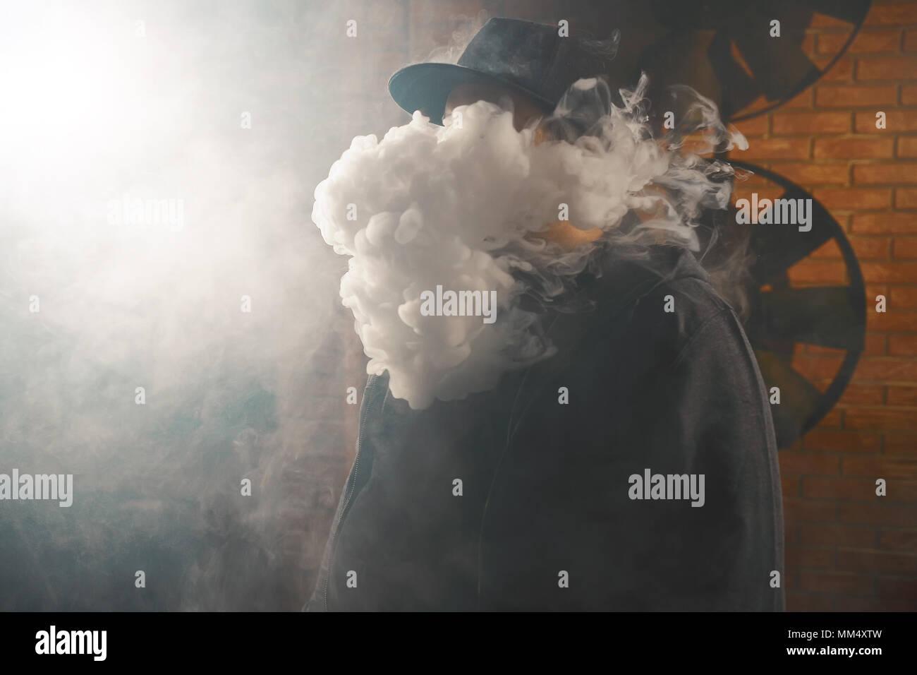 A cloud of vapor. Vaping man holding a mod. Brick background. Vape ...