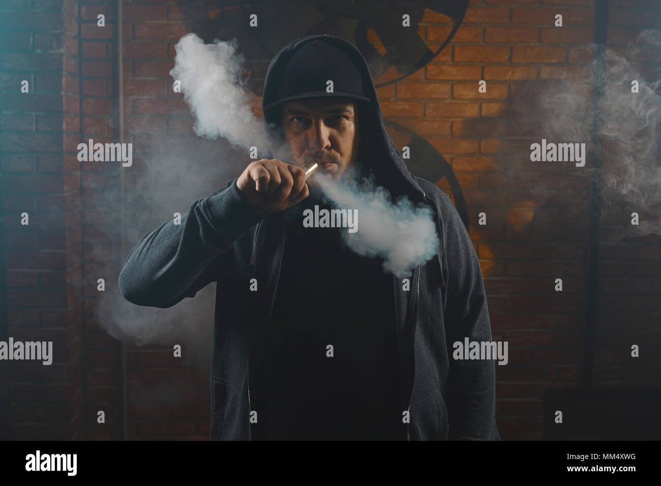 A cloud of vapor. Vaping man holding a mod. Brick background. Vape ...
