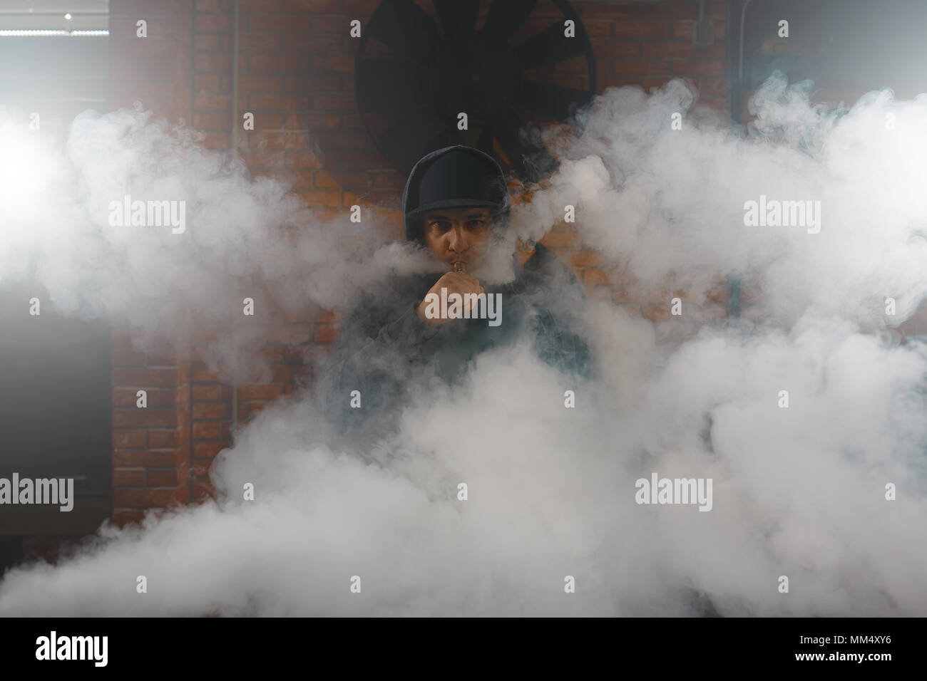 A cloud of vapor. Vaping man holding a mod. Brick background. Vape ...