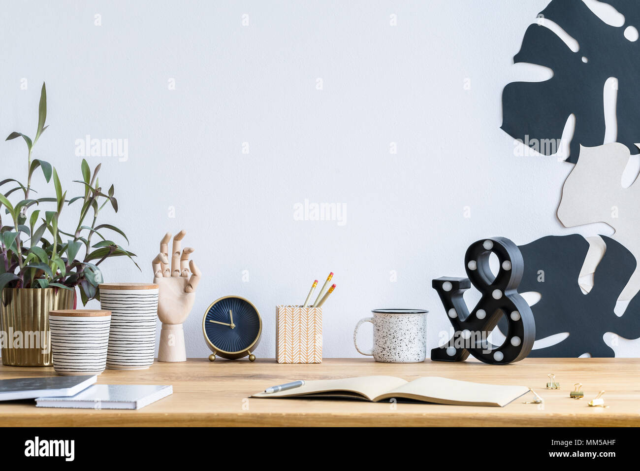 Messy desk with a plant in a golden pot, wooden hand, clock and leaves ...
