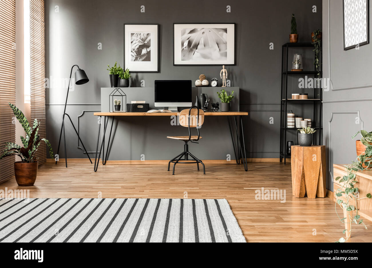 Plant on wooden stool near table with computer monitor in grey work ...
