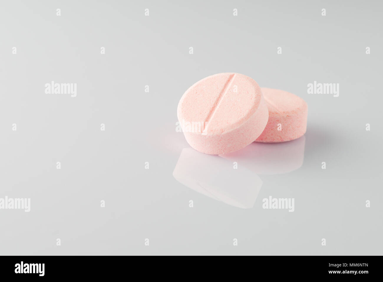 two pink medical ascorbic pills on a light background with reflection ...