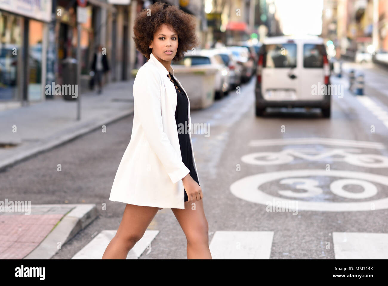 Young black woman with afro hairstyle walking on a crosswalk in an ...