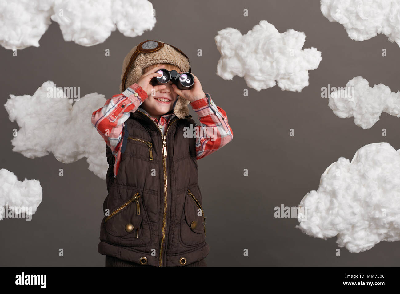 boy dressed as an airplane pilot stands between the clouds and looks ...