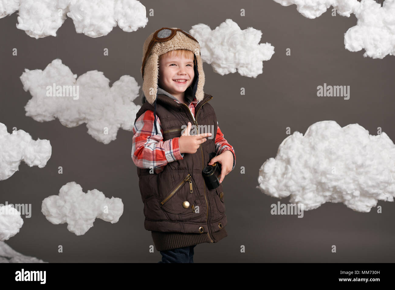 boy dressed as an airplane pilot stands between the clouds and looks ...