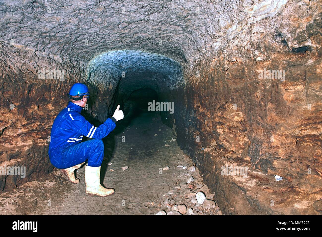 Man in underground tunnel works. Employee in safety suit works in ...