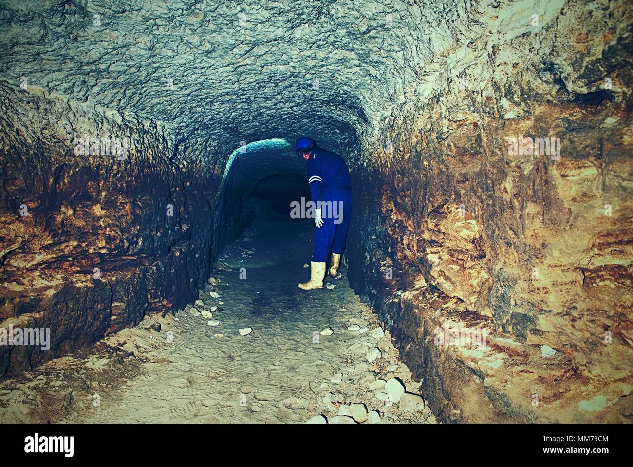 Underground work. Hunched worker in a blue overall and a safety helmet ...