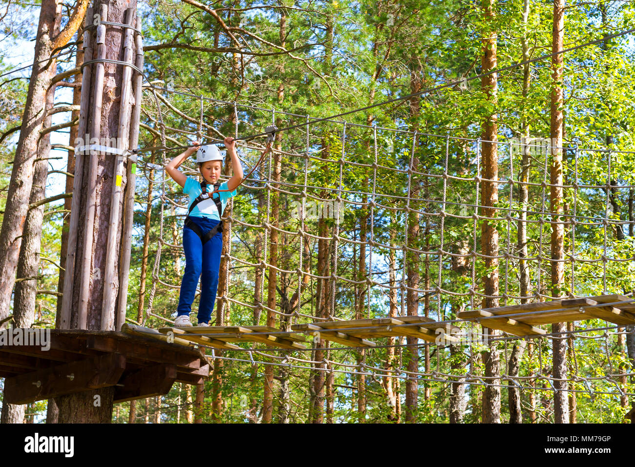 Teenage girl goes on hinged trail in extreme rope Park in summer forest ...
