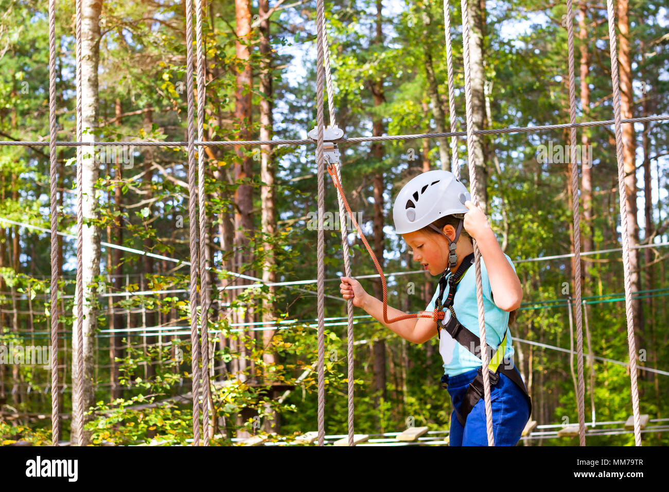 Teenage girl goes on hinged trail in extreme rope Park in summer forest ...