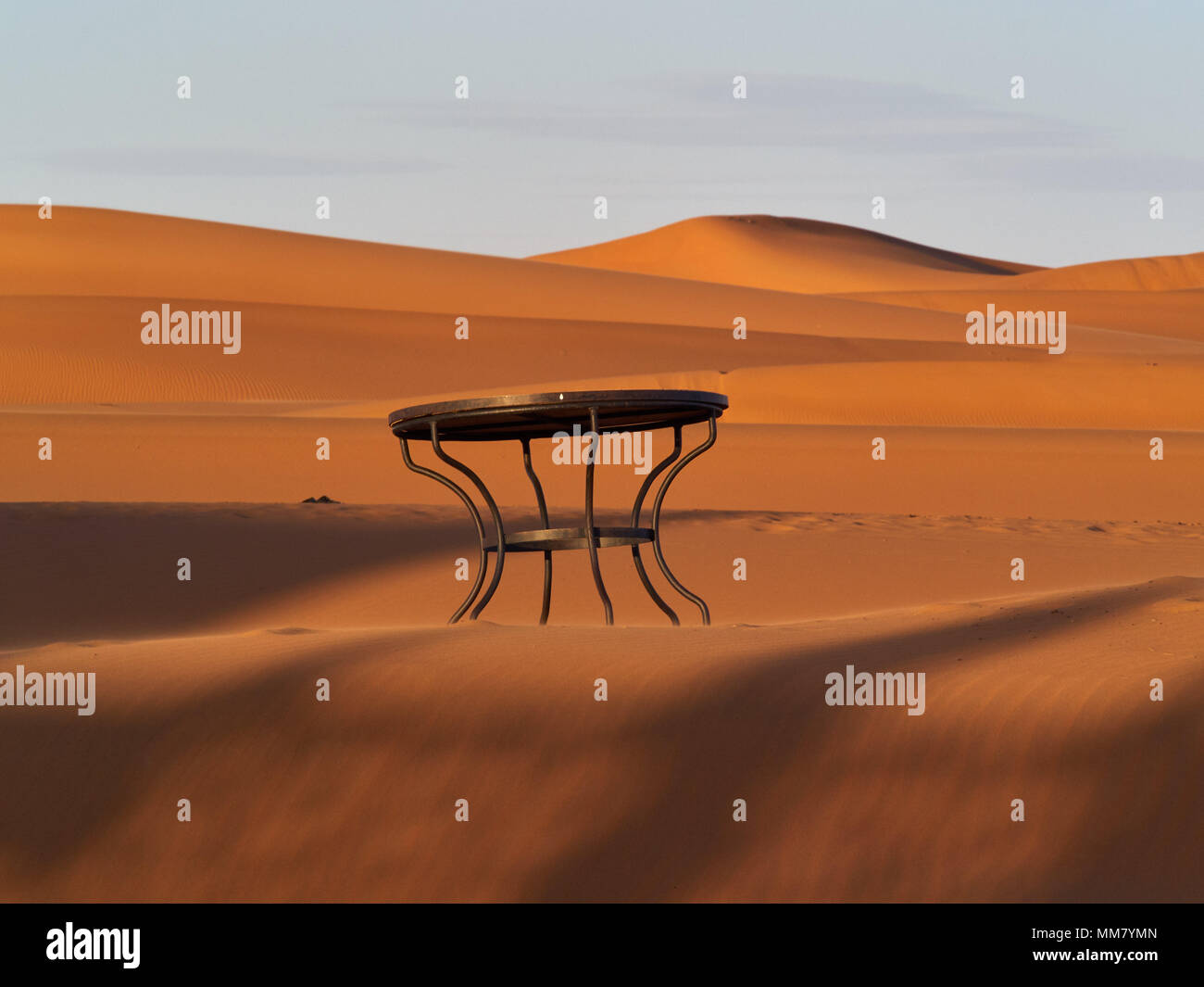 Round metal table on a small sand dune, evening in Merzouga, Sahara ...